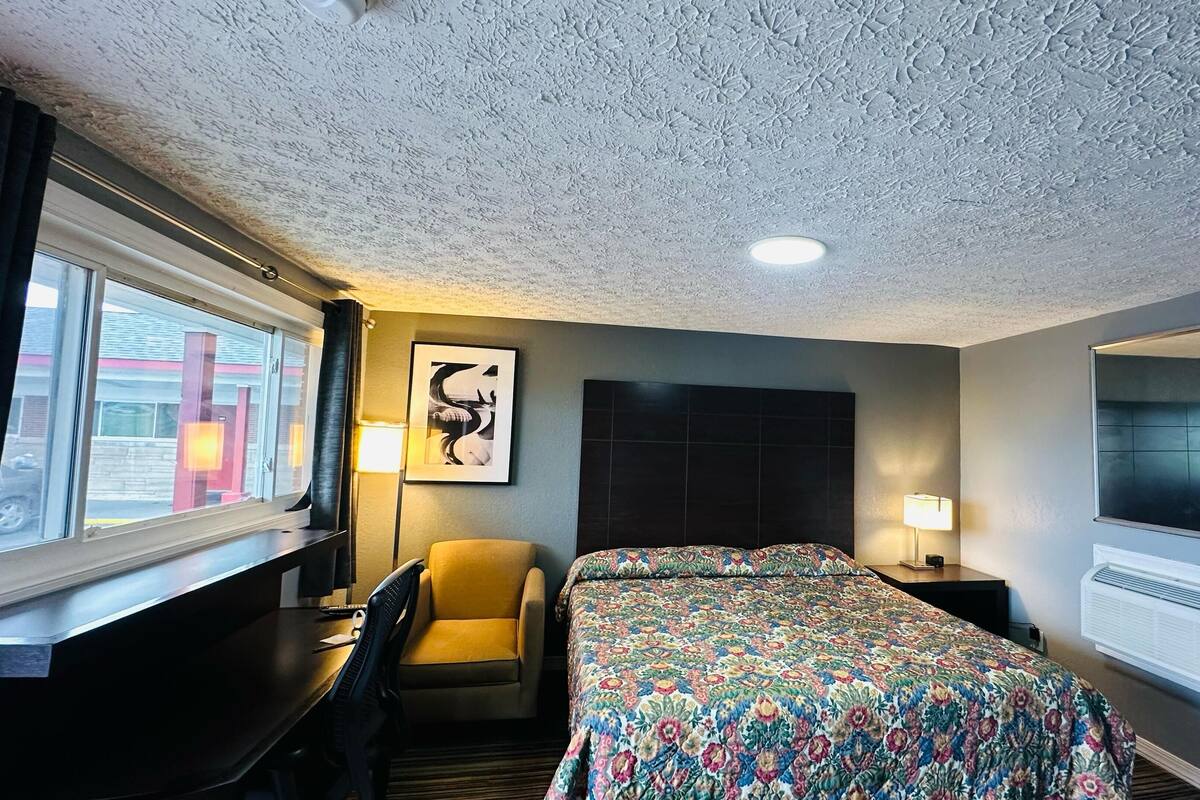 Quarto de hotel com cama, escrivaninha, cadeira, espelho grande e janela com vista para o exterior.