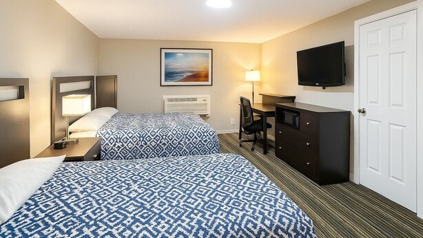 Quarto de hotel com duas camas, uma escrivaninha, uma cadeira, uma televisão e uma porta.