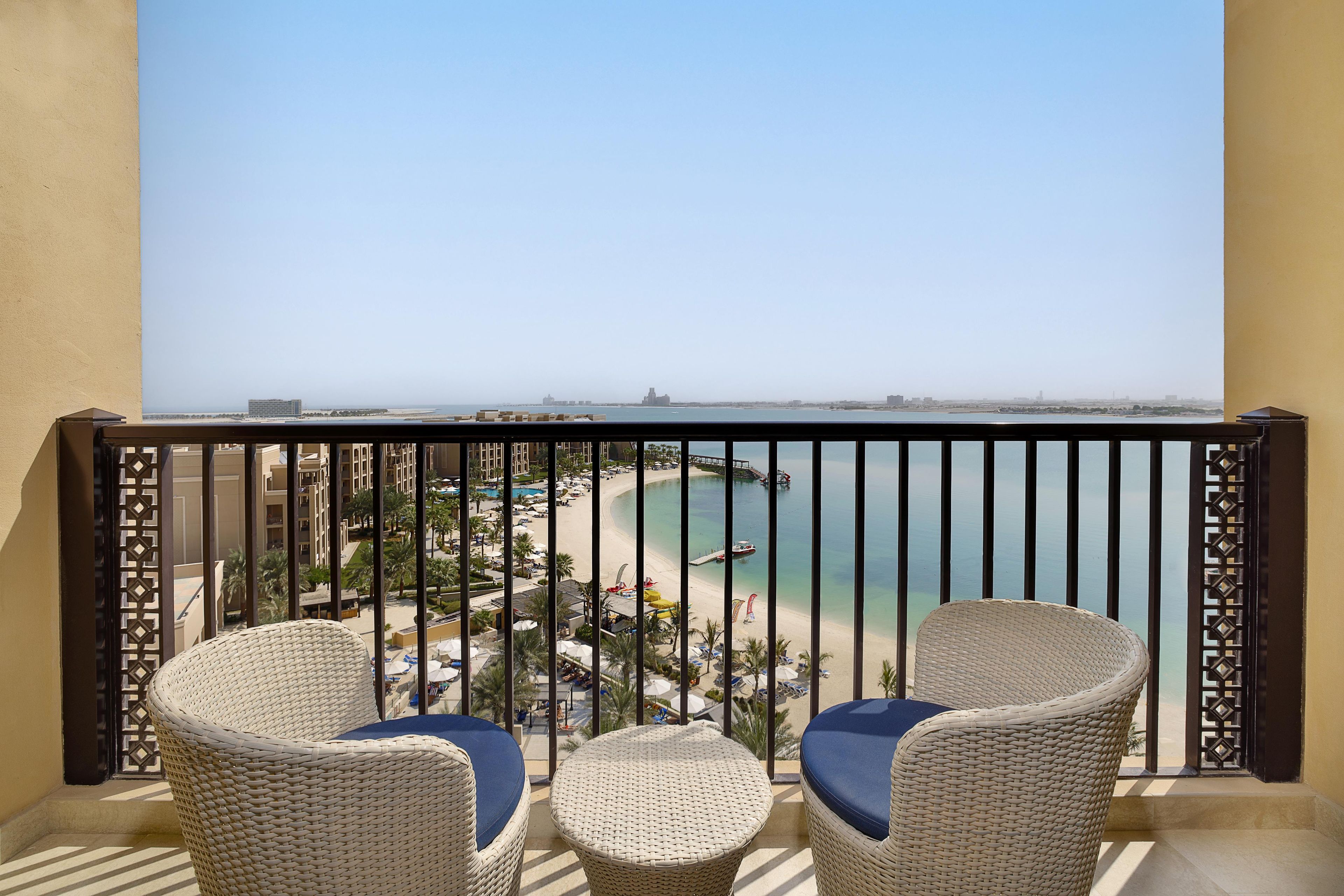 Varanda com mobiliário de vime com vista para uma praia e um porto de iates.