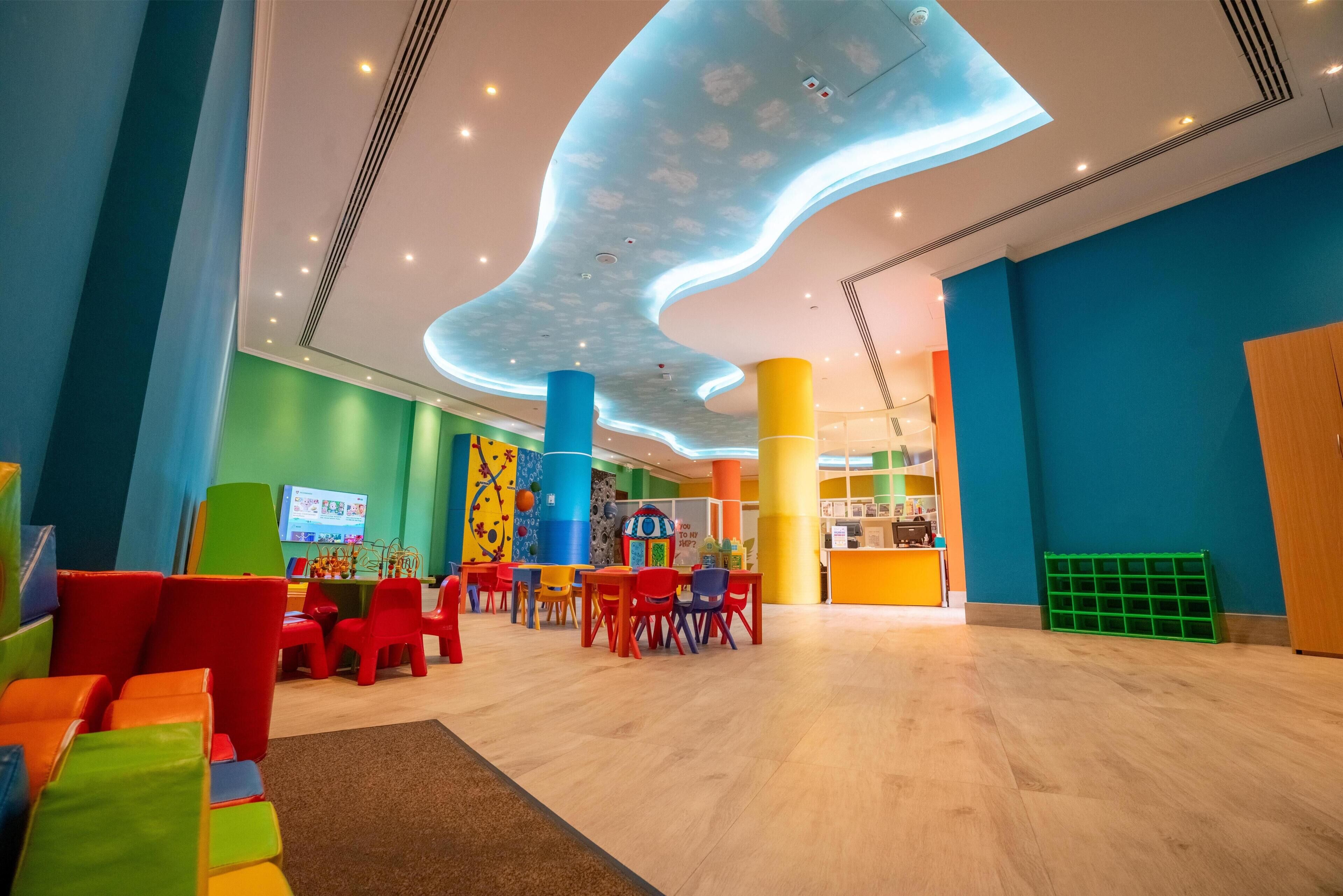 Um espaço interno bem iluminado, com design de teto moderno, áreas de estar coloridas e um balcão visível ao fundo.