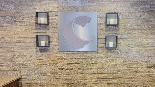 Paredes com uma grande letra 'C' iluminada e quatro luminárias fixadas.