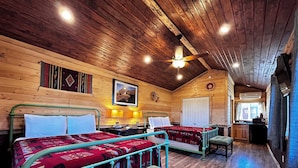 Um quarto acolhedor de cabana de madeira com duas camas, um banco, um ventilador de teto e um quadro na parede.