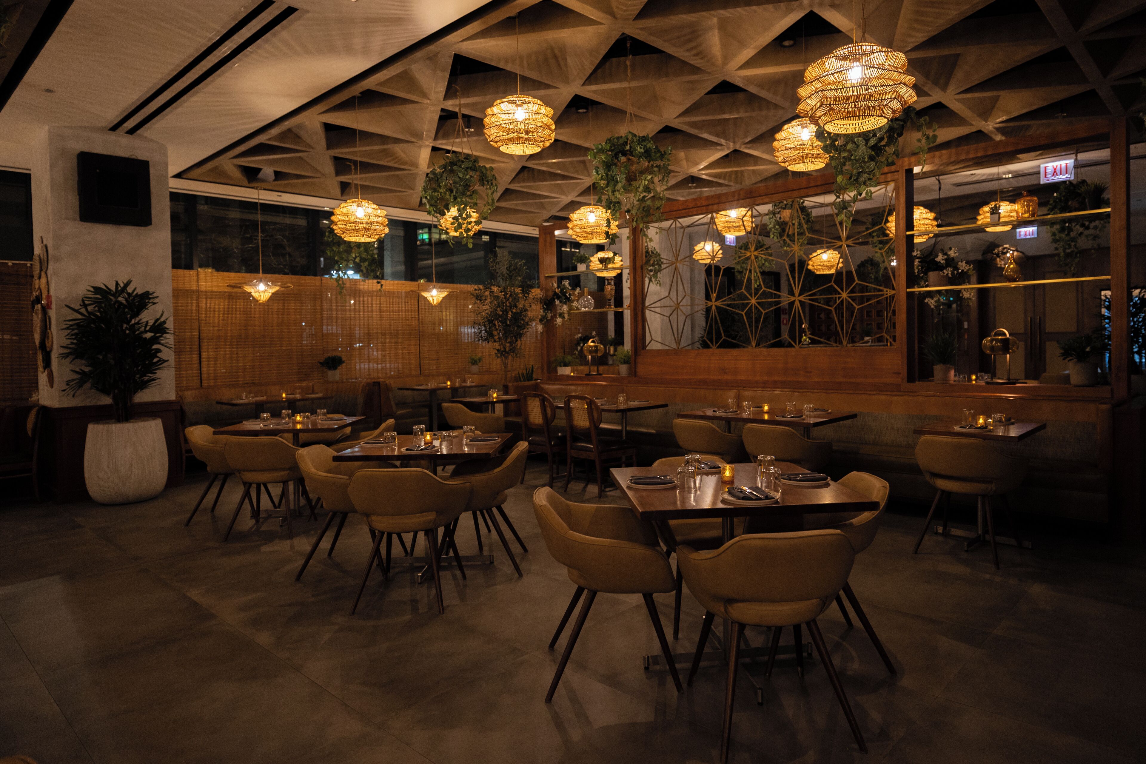 Interior de restaurante com várias mesas e cadeiras, luminárias pendentes e uma janela grande com vista.