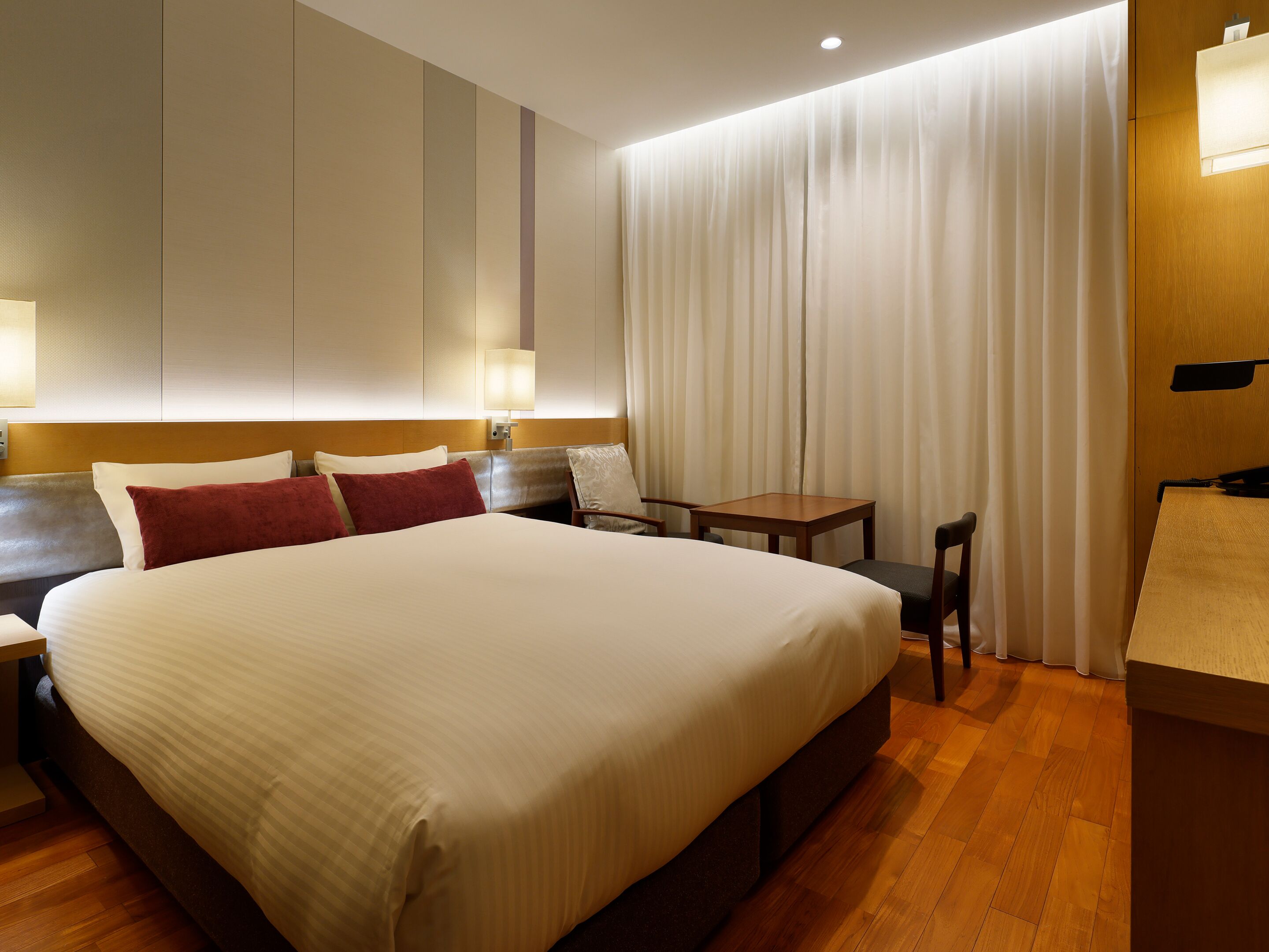 Quarto de hotel com uma cama grande, mesas de cabeceira, uma escrivaninha e uma cadeira.