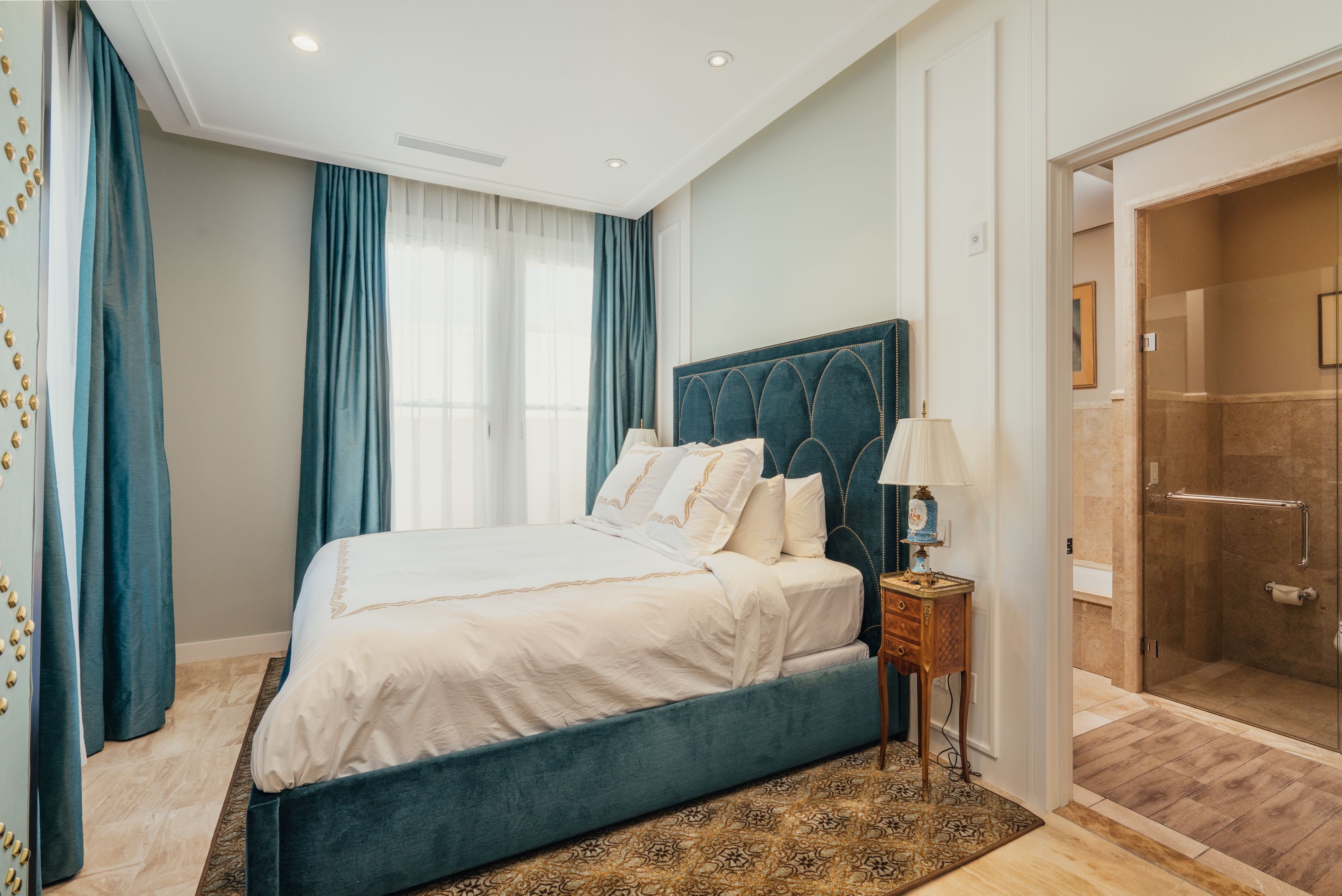 Quarto com cama grande, mesa de cabeceira, luminária e área de chuveiro.