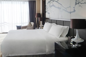 Quarto de hotel com uma cama grande, uma cadeira, uma mesa de cabeceira e um abajur.