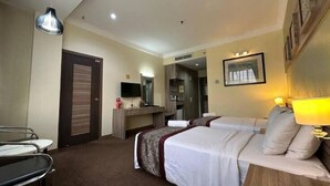 Quarto de hotel com cama, mesa de cabeceira, abajur, escrivaninha, cadeira e televisão.