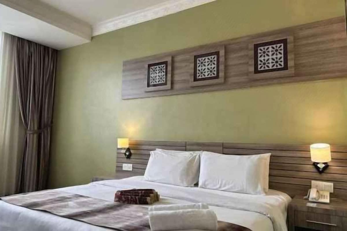 Quarto de hotel com uma cama, duas mesas de cabeceira e uma parede com painéis decorativos.