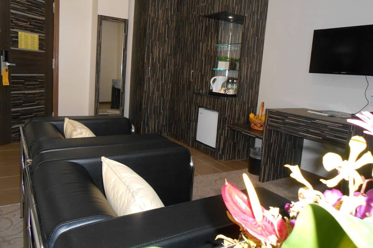 Uma sala de estar moderna com sofá, televisão, um frigorífico pequeno e um painel decorativo na parede.