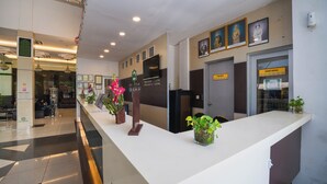 Área de recepção de hotel com balcão, quadros decorativos, televisão e placa indicativa da frente.