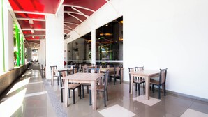 Um espaço amplo e interno, com várias mesas e cadeiras de madeira, piso ladrilhado e teto vermelho.