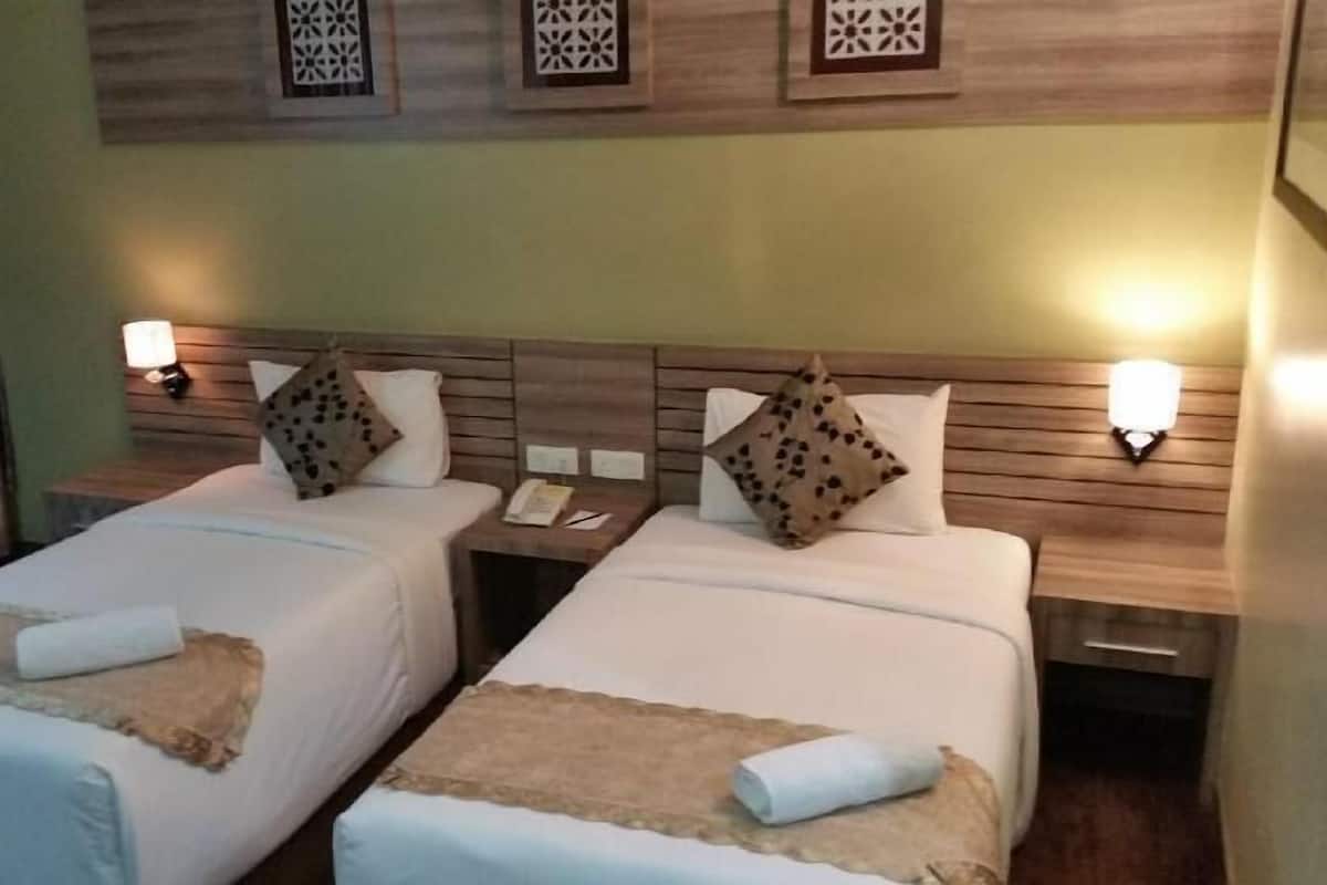 Quarto de hotel com duas camas de solteiro, mesas de cabeceira, luminárias e um painel decorativo na parede.