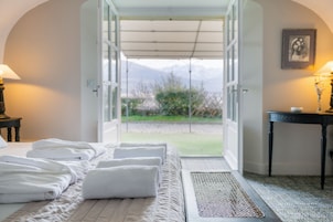 Quarto de hotel com uma cama, toalhas, uma mesa e vista para montanhas através de uma porta aberta.