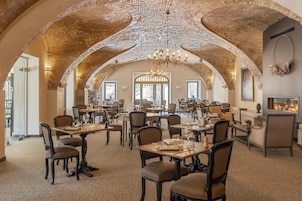 Uma ampla sala de jantar com tetos altos em arco e lustres, com várias mesas e cadeiras.