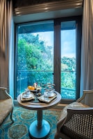 Varanda com mesa posta para chá, rodeada por cadeiras de vime, com vista para um jardim exuberante.
