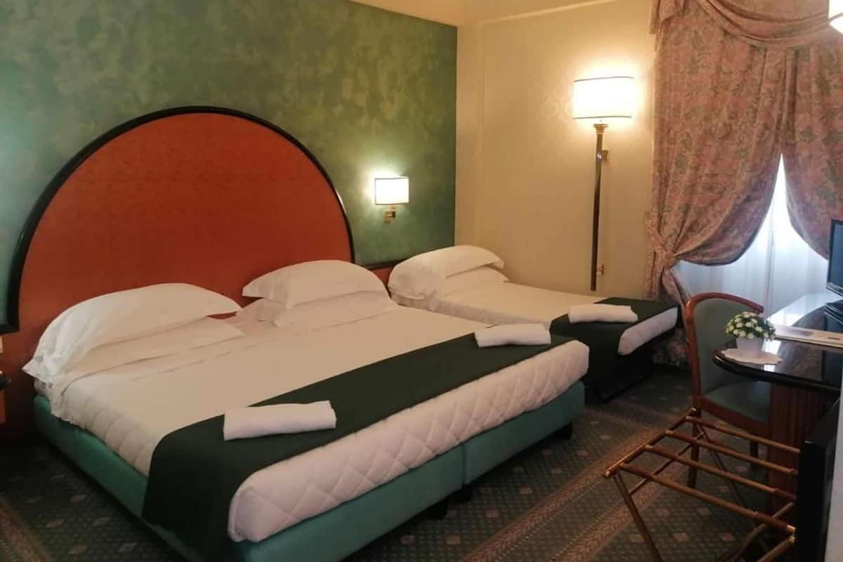 Quarto de hotel com duas camas, uma escrivaninha, uma cadeira e um abajur.