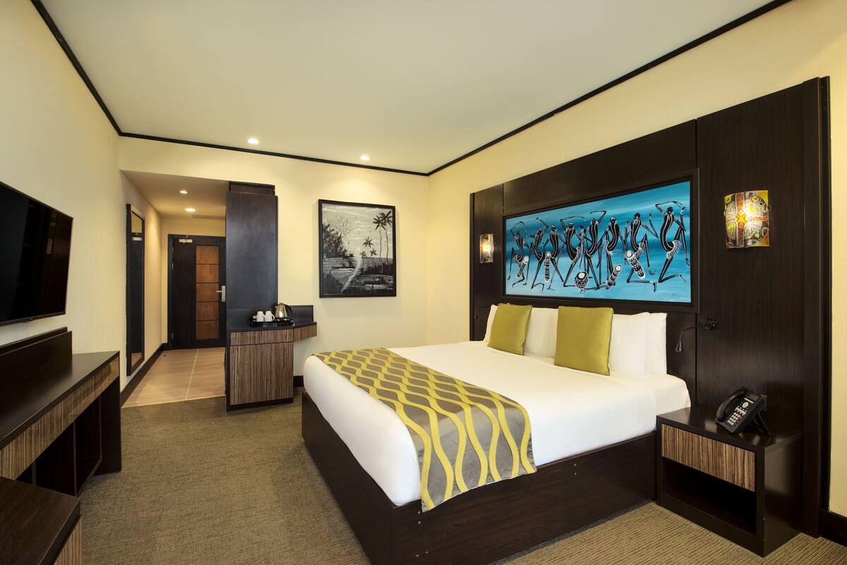 Quarto de hotel com uma cama grande, uma escrivaninha, uma televisão e obras de arte nas paredes.