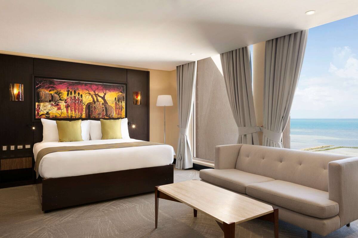 Quarto de hotel com uma cama grande, um sofá, uma mesinha e um quadro na parede.