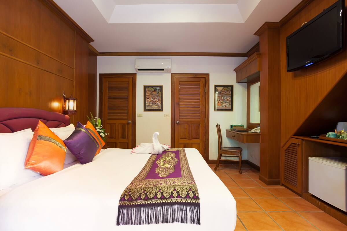 Quarto de hotel com cama, almofadas, um cisne decorativo, televisão e portas de madeira.