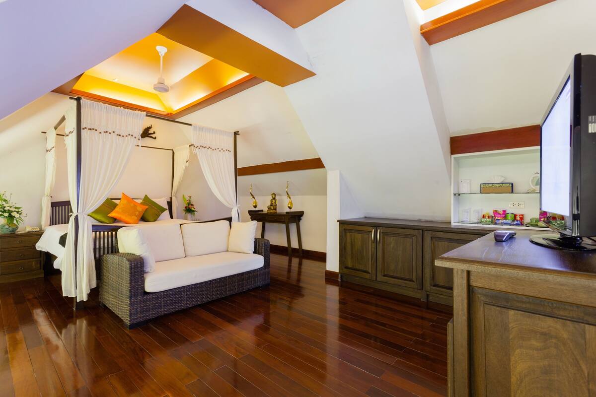 Quarto com cama de dossel, um sofá e televisão, numa área de cozinha moderna.