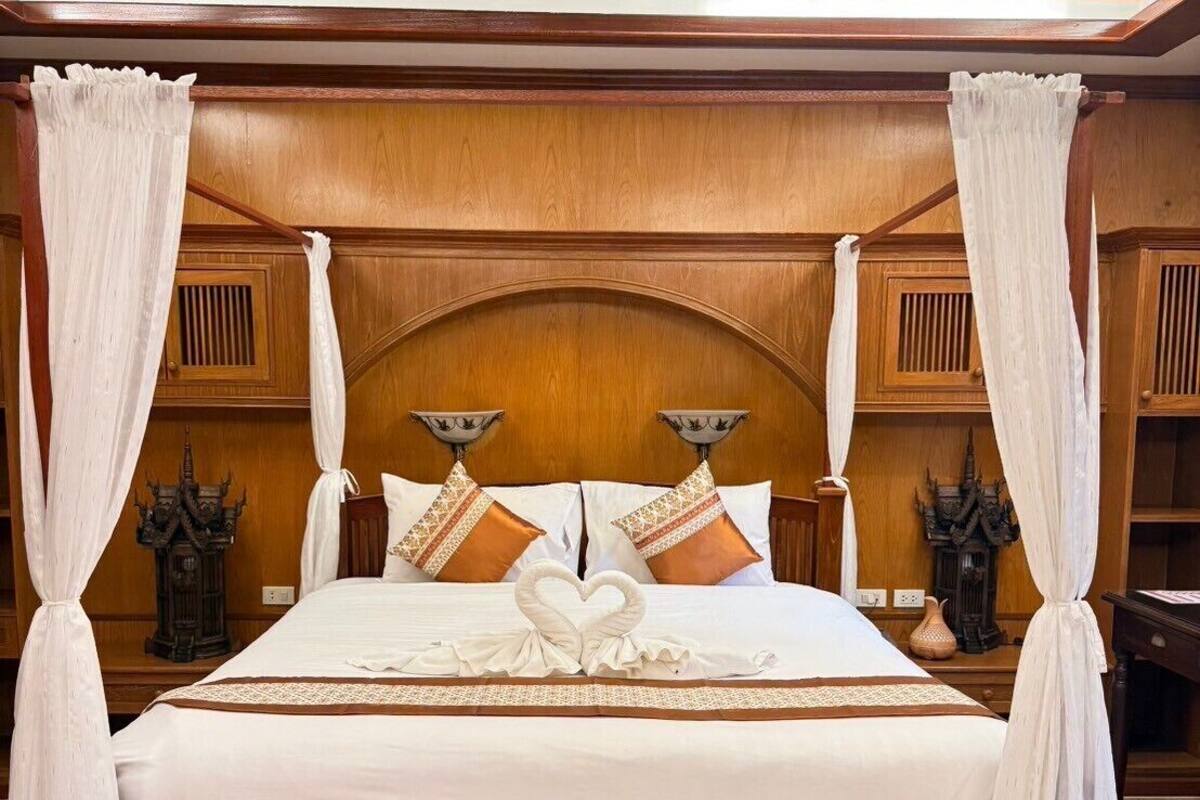 Uma cama grande e ricamente decorada, com cabeceira de madeira, roupa de cama branca e almofadas decorativas.