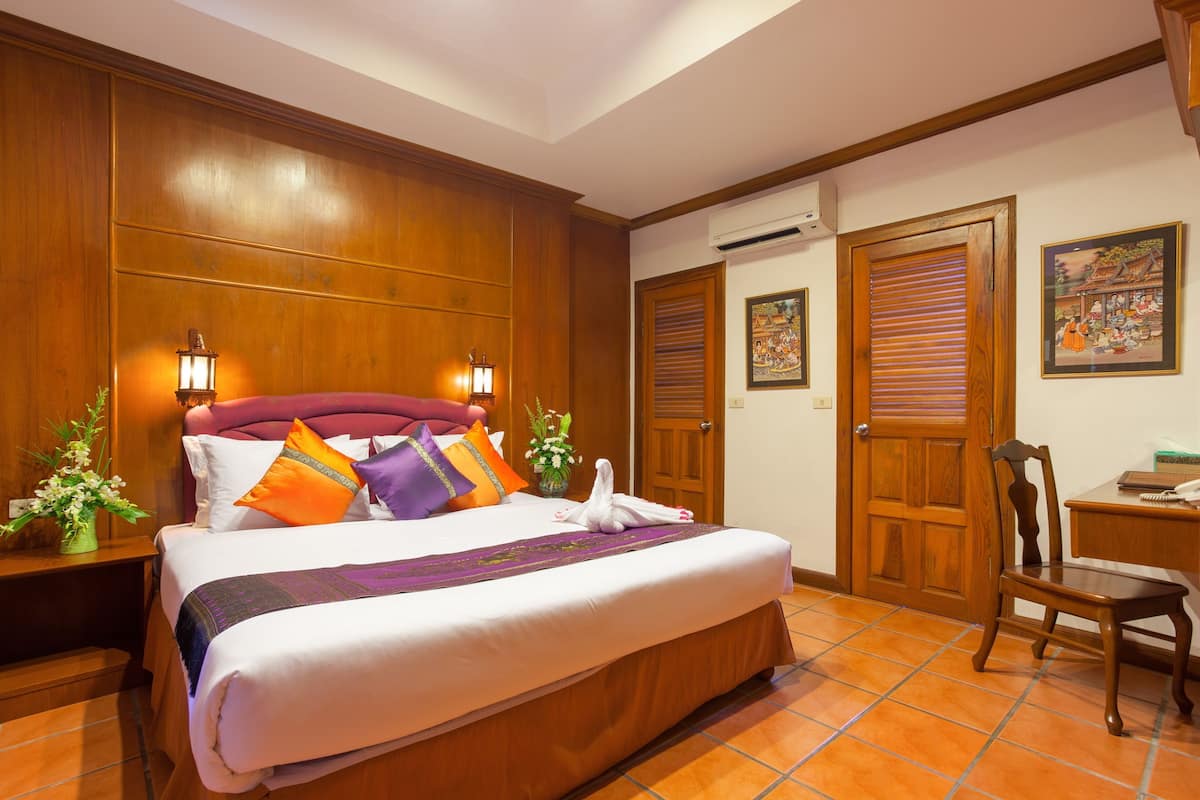Quarto de hotel com cama grande, cabeceira de madeira, duas luminárias de apoio, uma mesa de trabalho com cadeira e uma porta com janela.