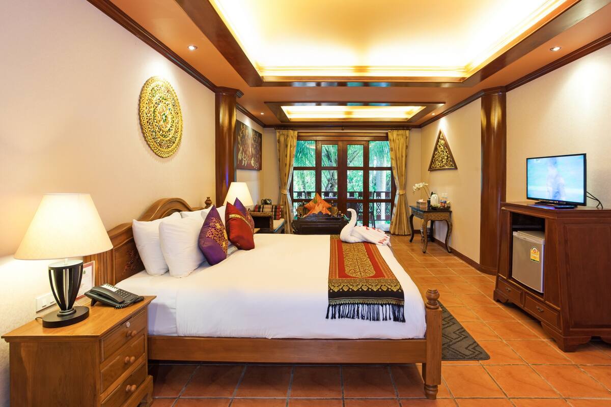 Quarto de hotel com uma cama grande, televisão, escrivaninha com luminária e um objeto decorativo na parede.