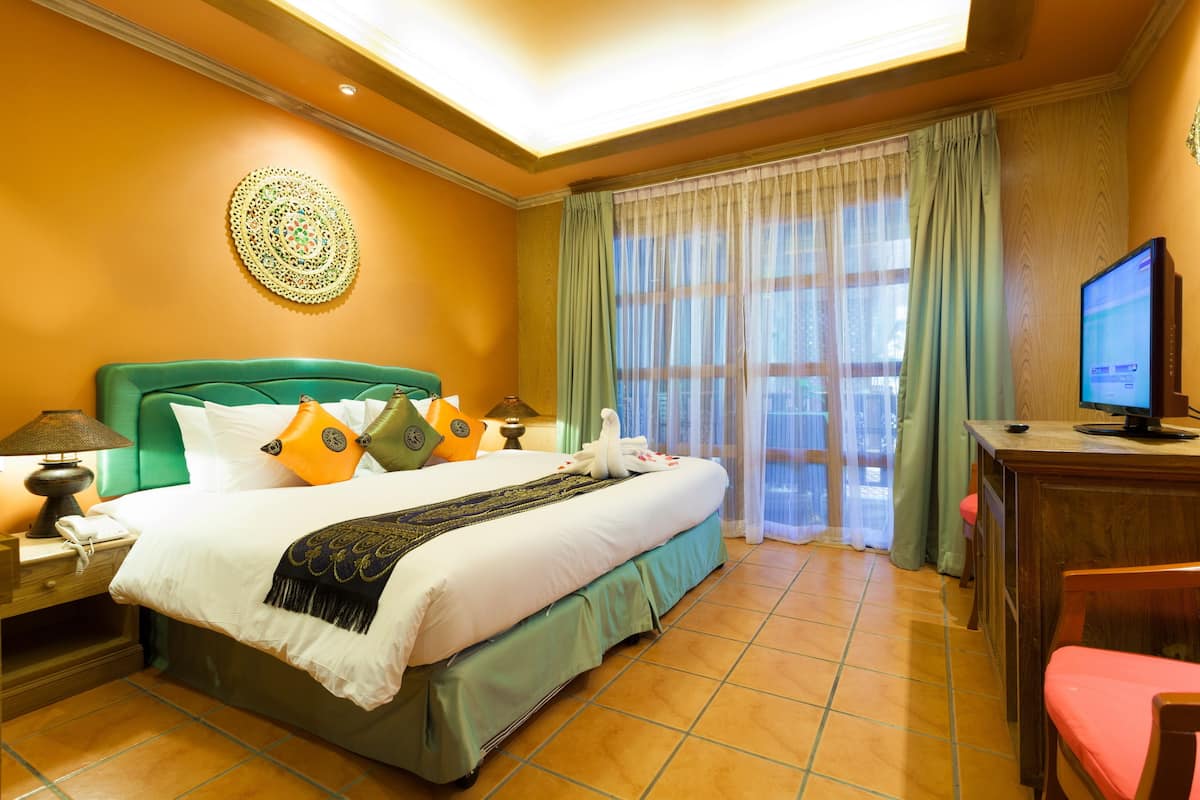 Quarto de hotel com uma cama grande, uma escrivaninha com computador, televisão e um painel decorativo na parede.