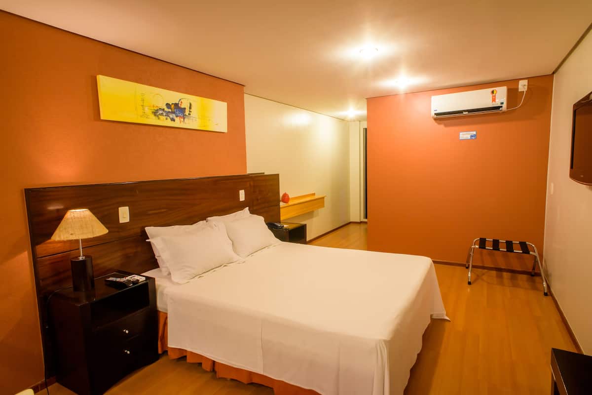 Quarto de hotel com cama, mesa de cabeceira, luminária, aparelho de ar condicionado e um quadro na parede.