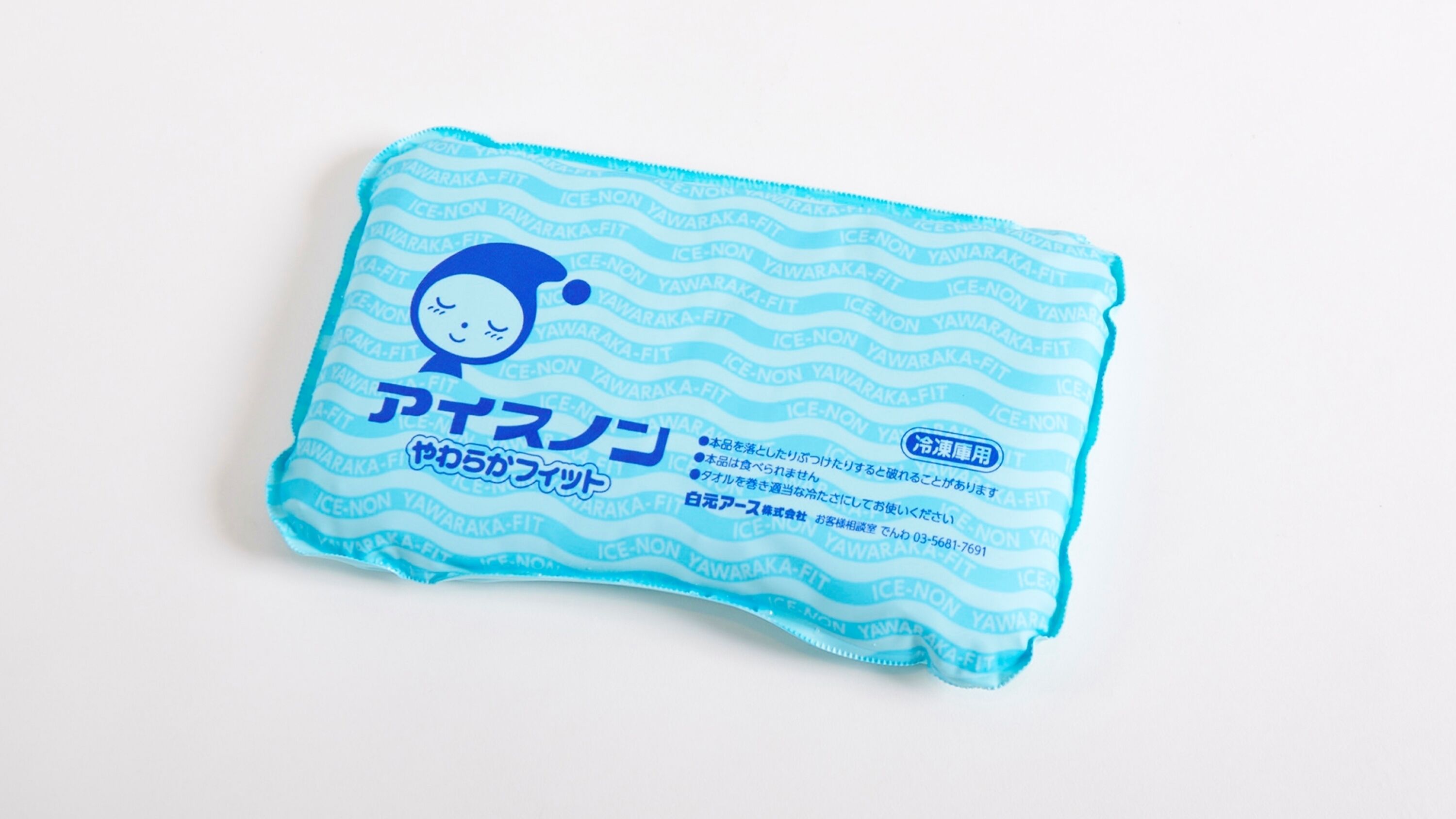 Almofada azul e branca com padrão, texto em japonês e um personagem de desenho animado.