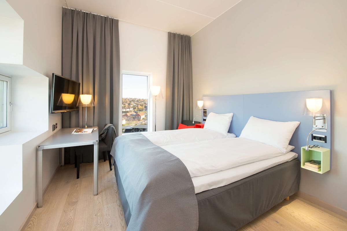 Quarto de hotel moderno com uma cama grande, uma escrivaninha, uma cadeira e uma televisão.