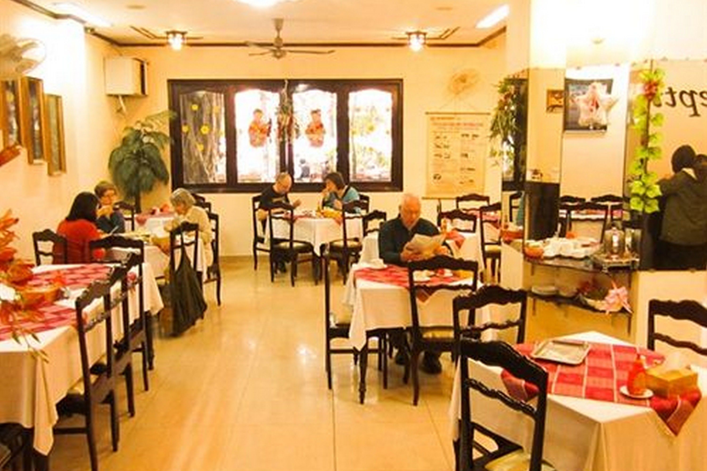Um restaurante com várias mesas e cadeiras, algumas com toalhas de mesa quadriculadas vermelhas e brancas.