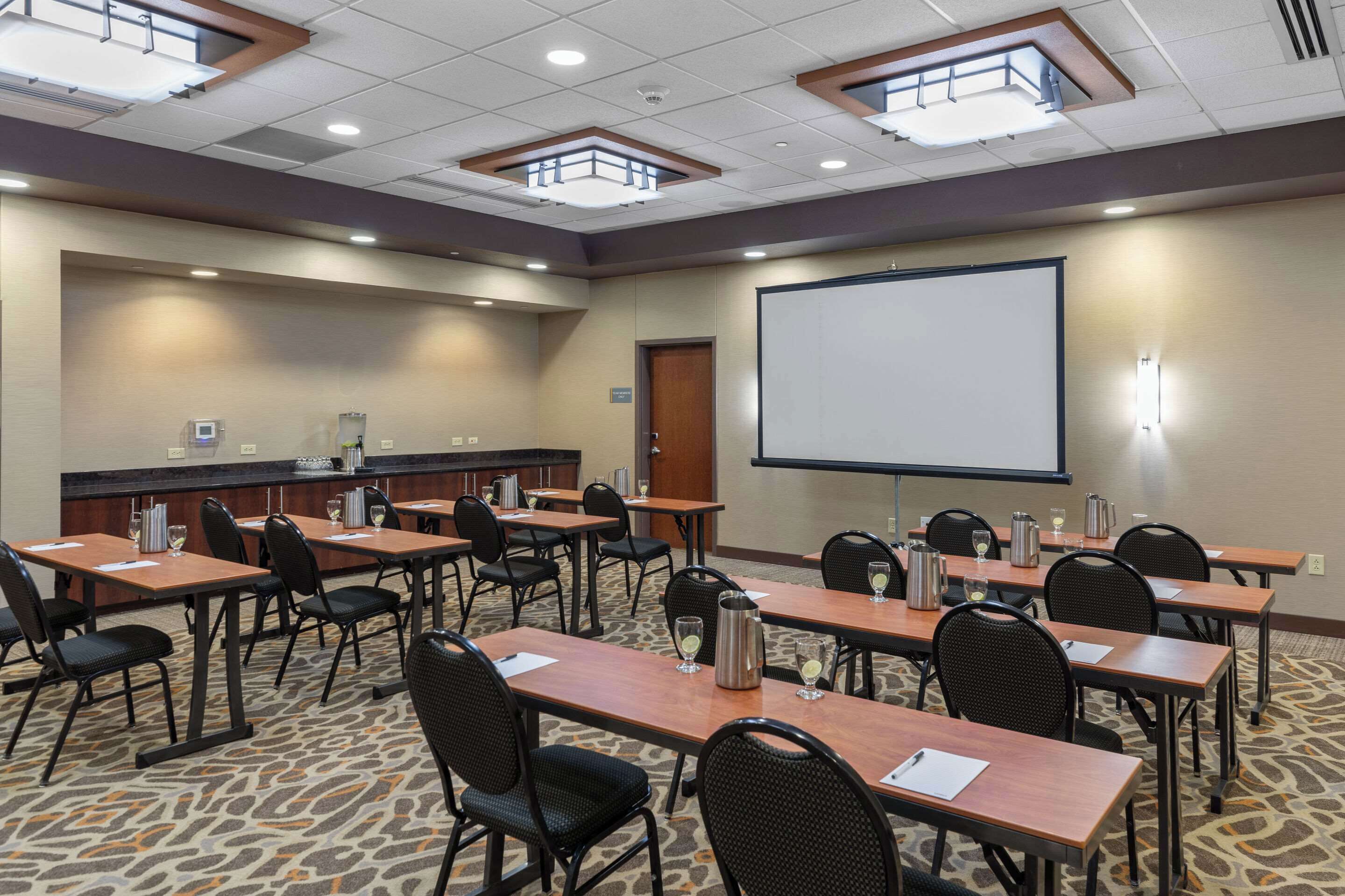 Uma sala de conferências com várias mesas, cadeiras, um projetor e um pódio.
