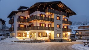 Um hotel com vários andares e varandas, uma entrada coberta de neve e uma placa com a inscrição "Dolomiten".