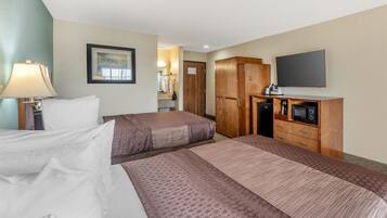 Quarto de hotel com duas camas, televisão, secretária com micro-ondas e casa de banho visível ao fundo.