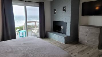 Quarto com cama grande, lareira, televisão e vista para o oceano.