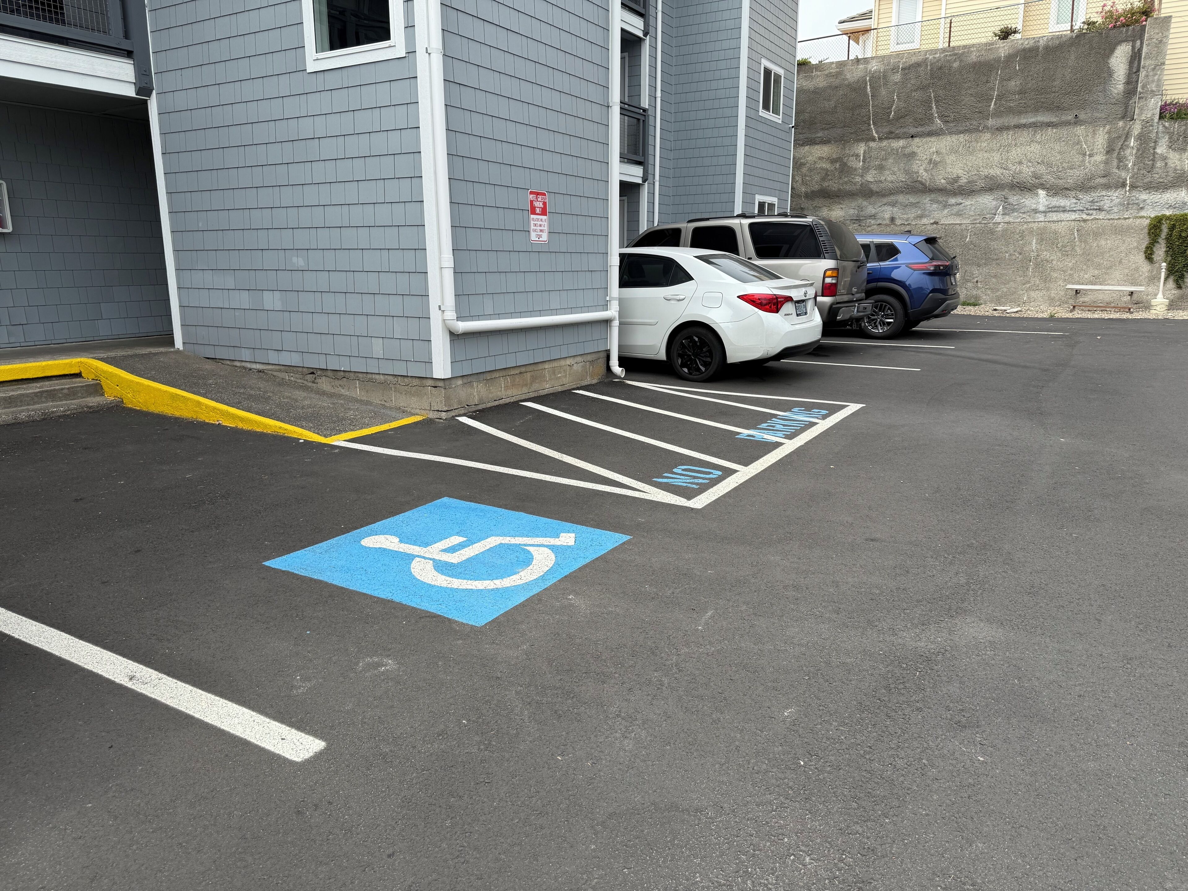 Um estacionamento com vagas demarcadas para pessoas com deficiência e um edifício com fachada cinzenta.