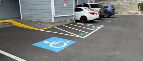 Um estacionamento com vagas demarcadas para pessoas com deficiência e um edifício com fachada cinzenta.