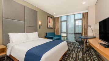 Quarto de hotel com uma cama grande, uma escrivaninha com computador, uma cadeira e uma televisão.
