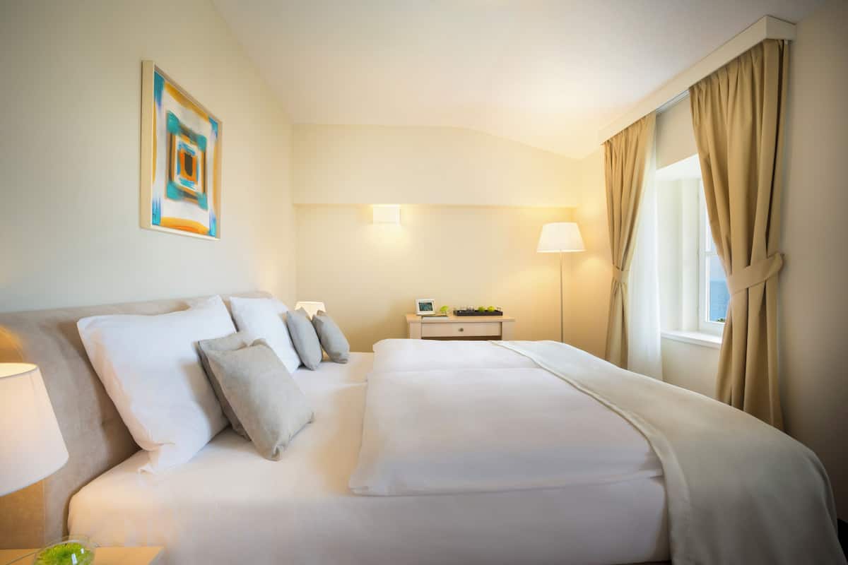 Quarto de hotel com cama, mesa de cabeceira, abajur e um quadro na parede.