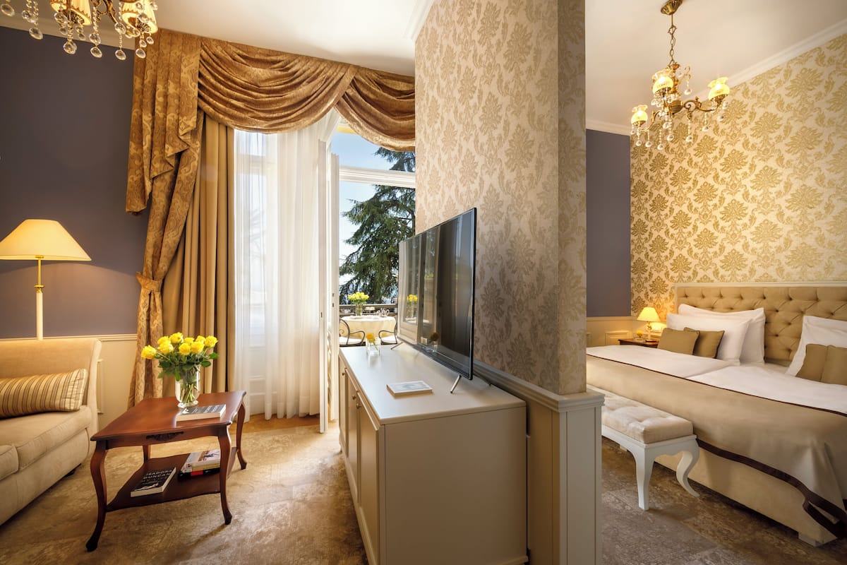 Quarto de hotel com uma cama grande, televisão, escrivaninha com abajur, sofá e vista para o exterior.