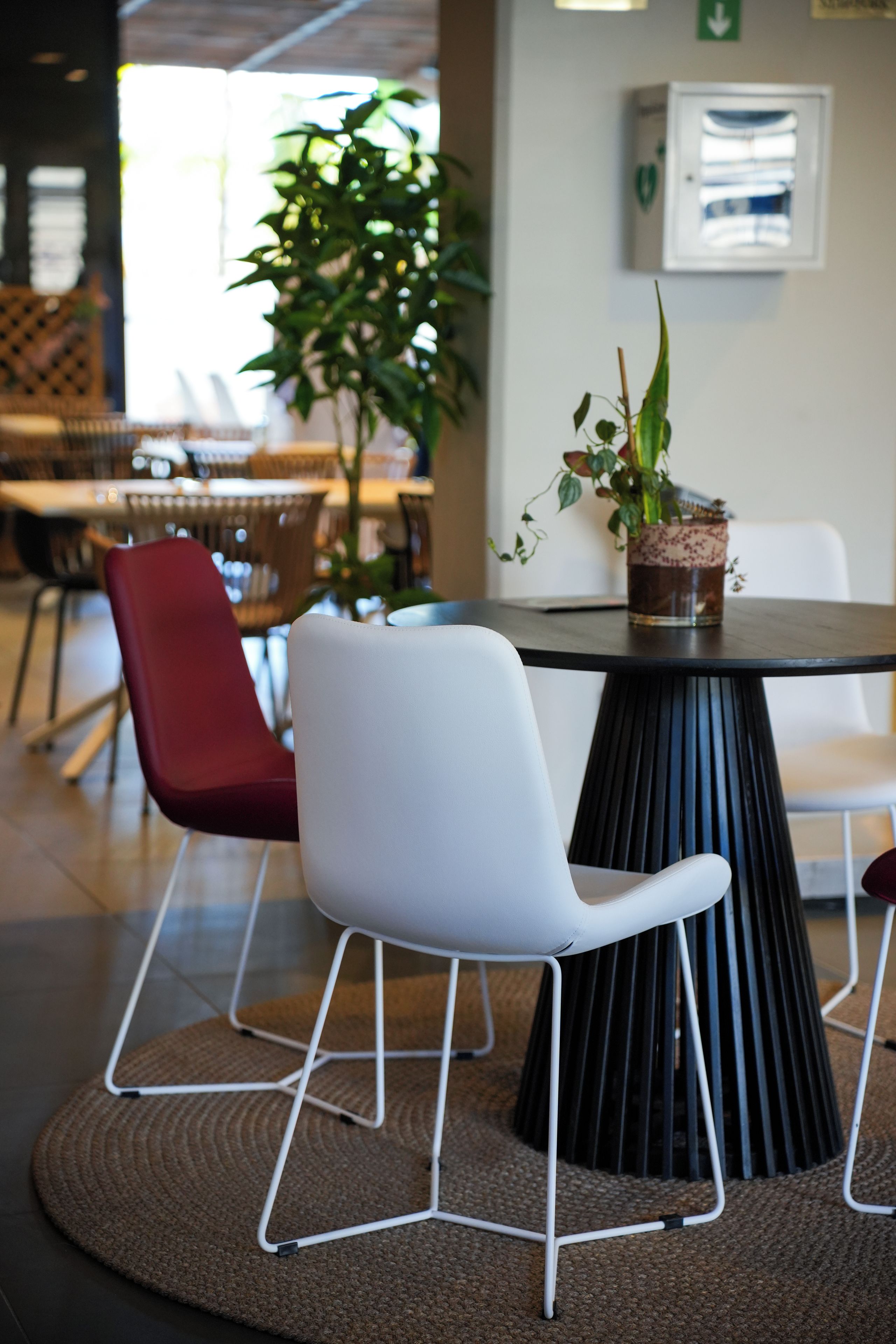 Uma sala de jantar moderna com mesa redonda, cadeiras brancas e vermelhas, e um vaso de planta.