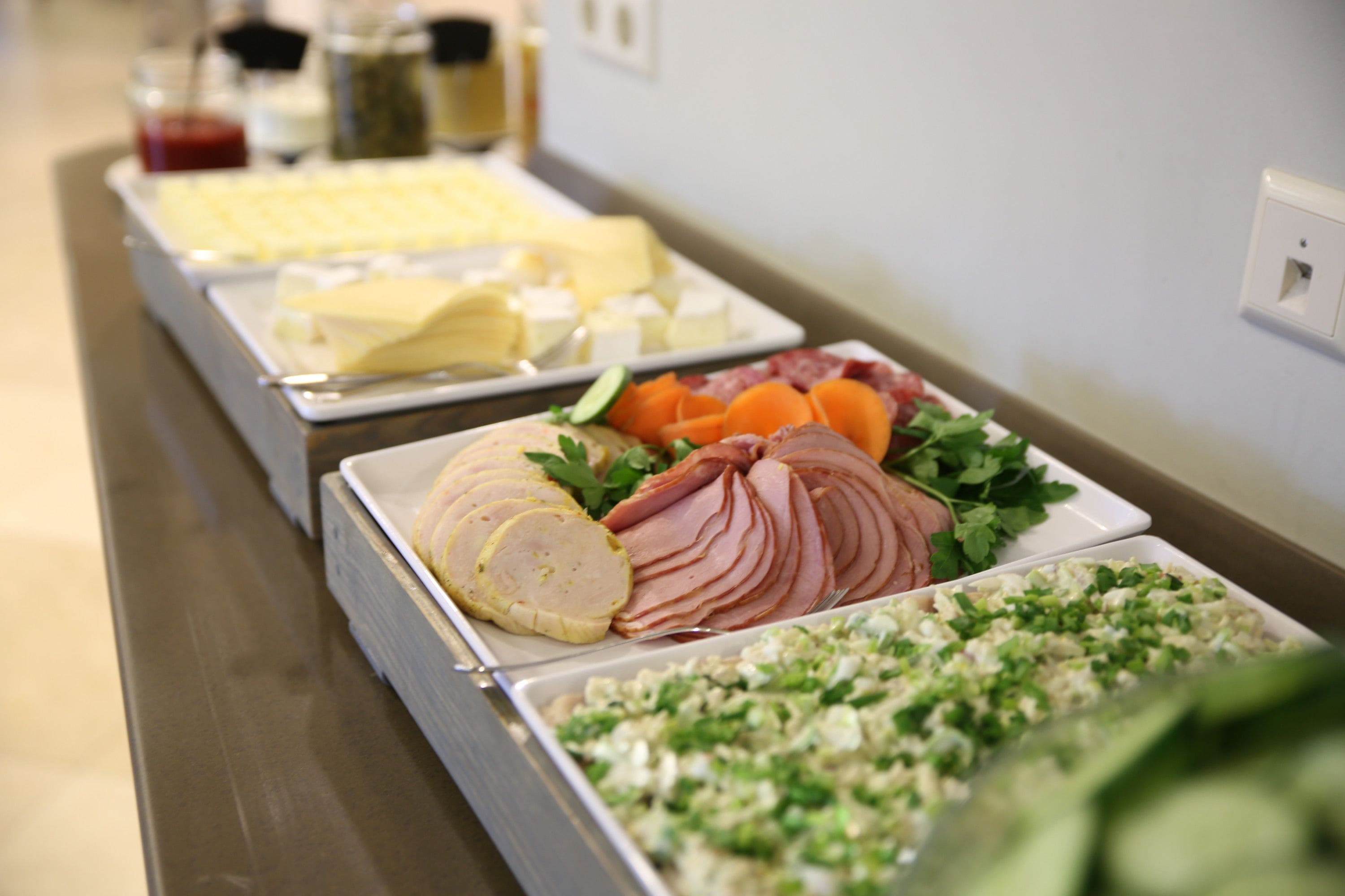 Buffet com diversos alimentos, incluindo carnes fatiadas, queijos e uma salada.