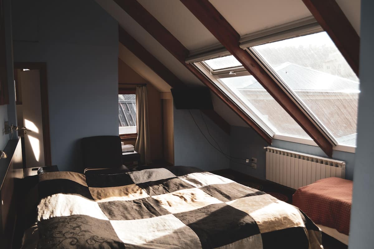 Um quarto com claraboia, cama, poltrona e radiador.