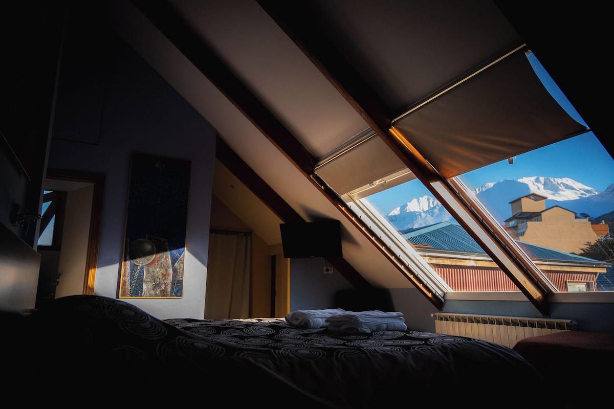 Quarto com claraboia, uma cama, TV de tela plana e vista para montanhas cobertas de neve.