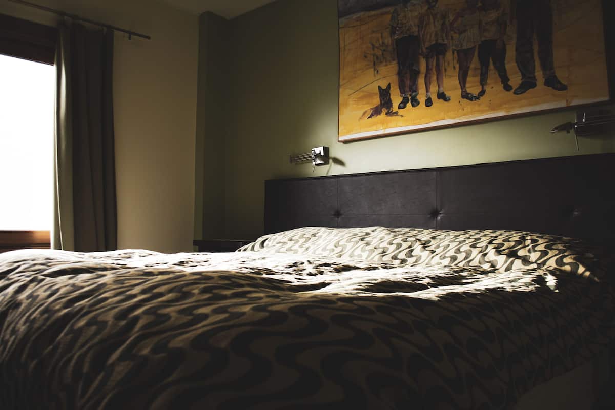 Quarto com cama, cabeceira, pintura e janela com cortinas.