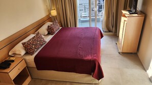 Quarto de hotel com cama, escrivaninha, televisão e vista para o exterior.
