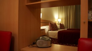 Quarto de hotel com uma cama, mesa de cabeceira com luminária e uma cadeira vermelha.
