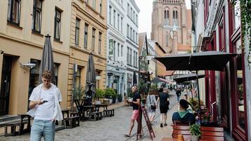Rua de paralelepípedos com mesas ao ar livre, uma torre de igreja ao fundo e pedestres.