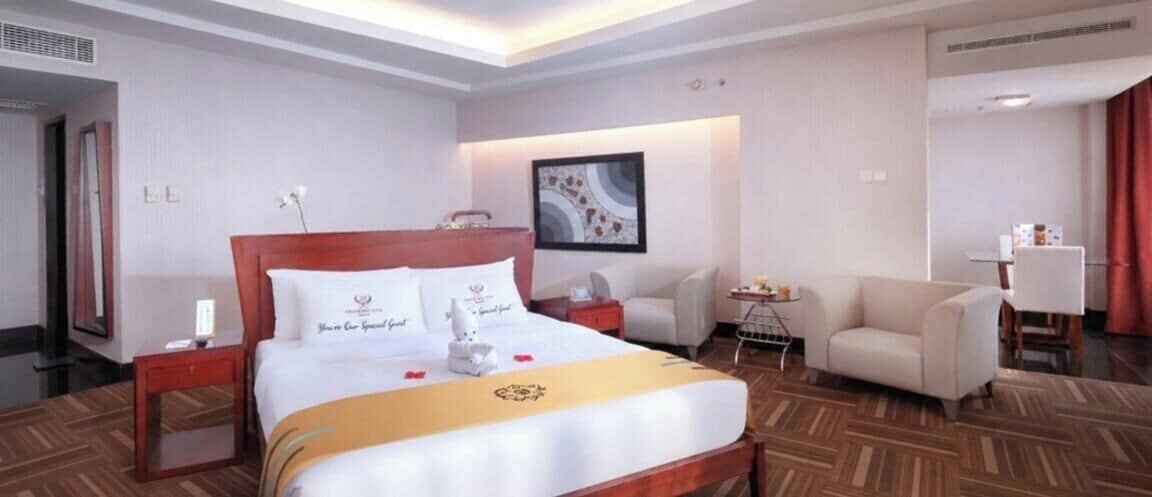 Quarto de hotel com uma cama grande, uma escrivaninha, uma cadeira e uma mesinha.